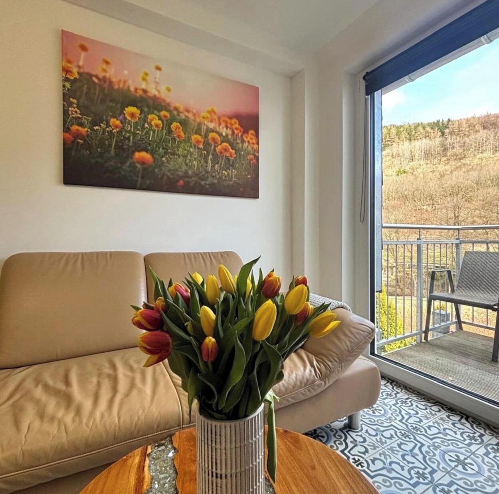 Uma sala de estar com um sofá, uma mesa de centro com um vaso de tulipas e um quadro de flores na parede.