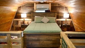 Um quarto no estilo loft com teto inclinado, paredes de madeira, cama com roupa de cama verde, duas luminárias de cabeceira e teto suspenso.