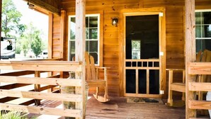 Uma cabana de madeira com varanda, porta com janela e uma mesa pequena.