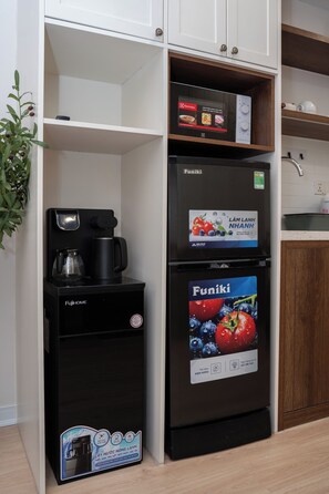 Uma cozinha compacta com geladeira preta, cafeteira e um pequeno armário com micro-ondas.