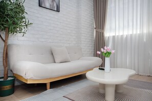 Uma sala de estar moderna com um sofá branco, uma mesinha redonda com um vaso de flores e uma planta em vaso.