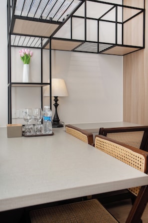 Quarto de hotel com mesa de jantar, cadeiras, abajur, vaso com flores e garrafa de água.