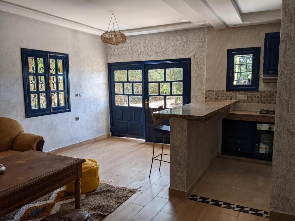 Uma sala de estar ampla com sofá, mesa de centro e tapete. Há uma cozinha com bancada e armários.