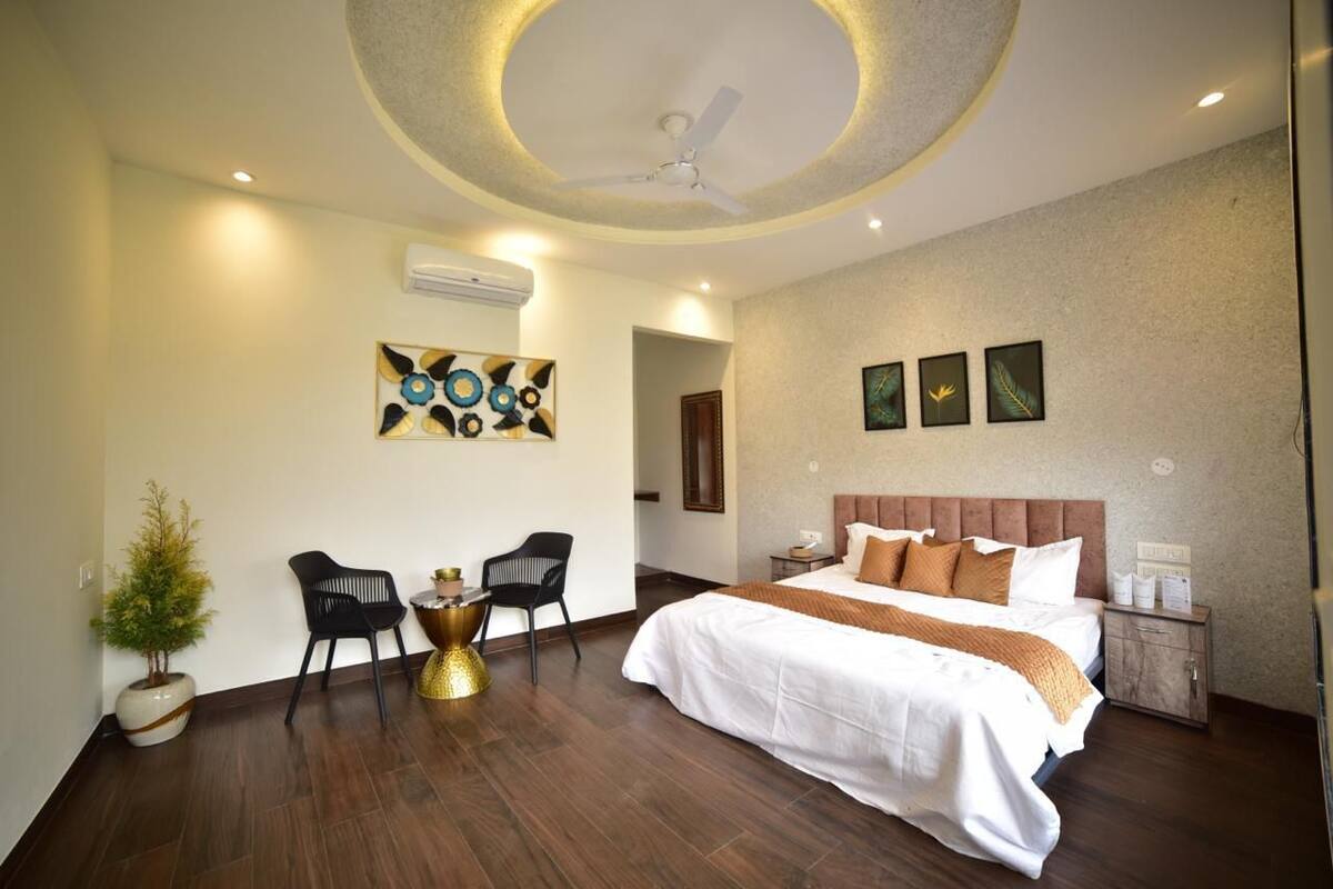 Quarto de hotel com uma cama grande, um ventilador de teto, uma mesinha com cadeiras e obras de arte nas paredes.