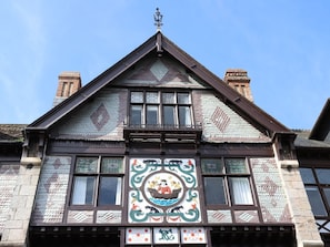 Um edifício com telhado triangular, azulejos decorativos e um emblema em destaque com um barco e figuras.