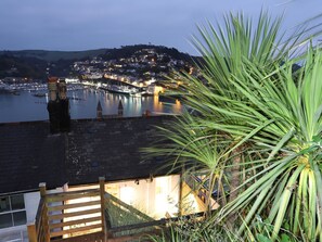 Uma vila costeira ao entardecer, com um porto, uma escadaria de madeira e uma palmeira.