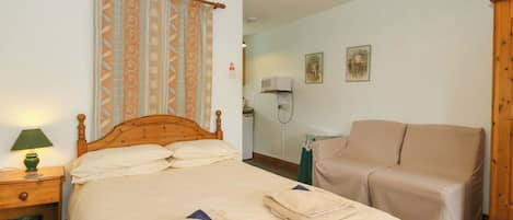 Quarto com cama, mesa de cabeceira com abajur, cadeira, escrivaninha com computador e aquecedor fixado na parede.