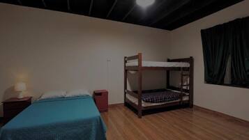 Quarto com cama de solteiro, beliche, mesa de cabeceira, luminária e janela com cortinas.