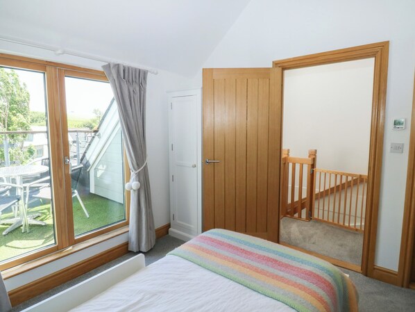 Quarto com cama, janela com cortinas, porta e vista para área externa com mesa e cadeiras.