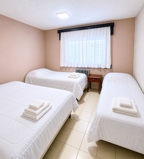 Quarto de hotel com duas camas de solteiro, uma escrivaninha pequena e uma janela com cortinas.
