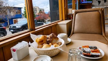 Uma área de refeições com uma mesa posta para o café da manhã, incluindo croissants, doces e um prato de geleia. Há duas xícaras, um copo e uma colher na mesa.