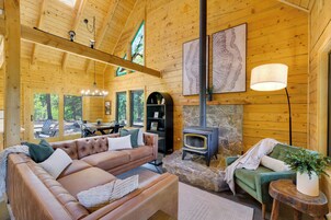 Interior acolhedor de uma cabana com um sofá de couro, lareira de pedra e área de jantar.