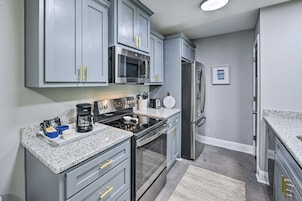 Cozinha moderna com armários cinza, eletrodomésticos de aço inoxidável e bancadas de granito.