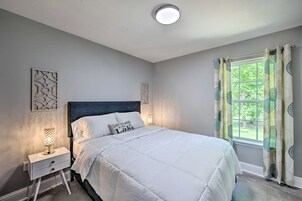 Quarto com cama, mesa de cabeceira e janela com cortinas.