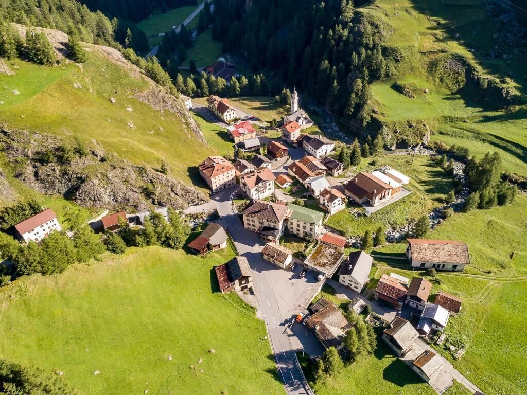 Vista aérea de uma aldeia com edifícios, estradas e colinas verdes.