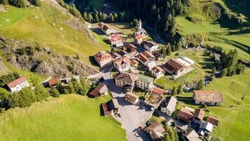 Vista aérea de uma aldeia com edifícios, estradas e colinas verdes.