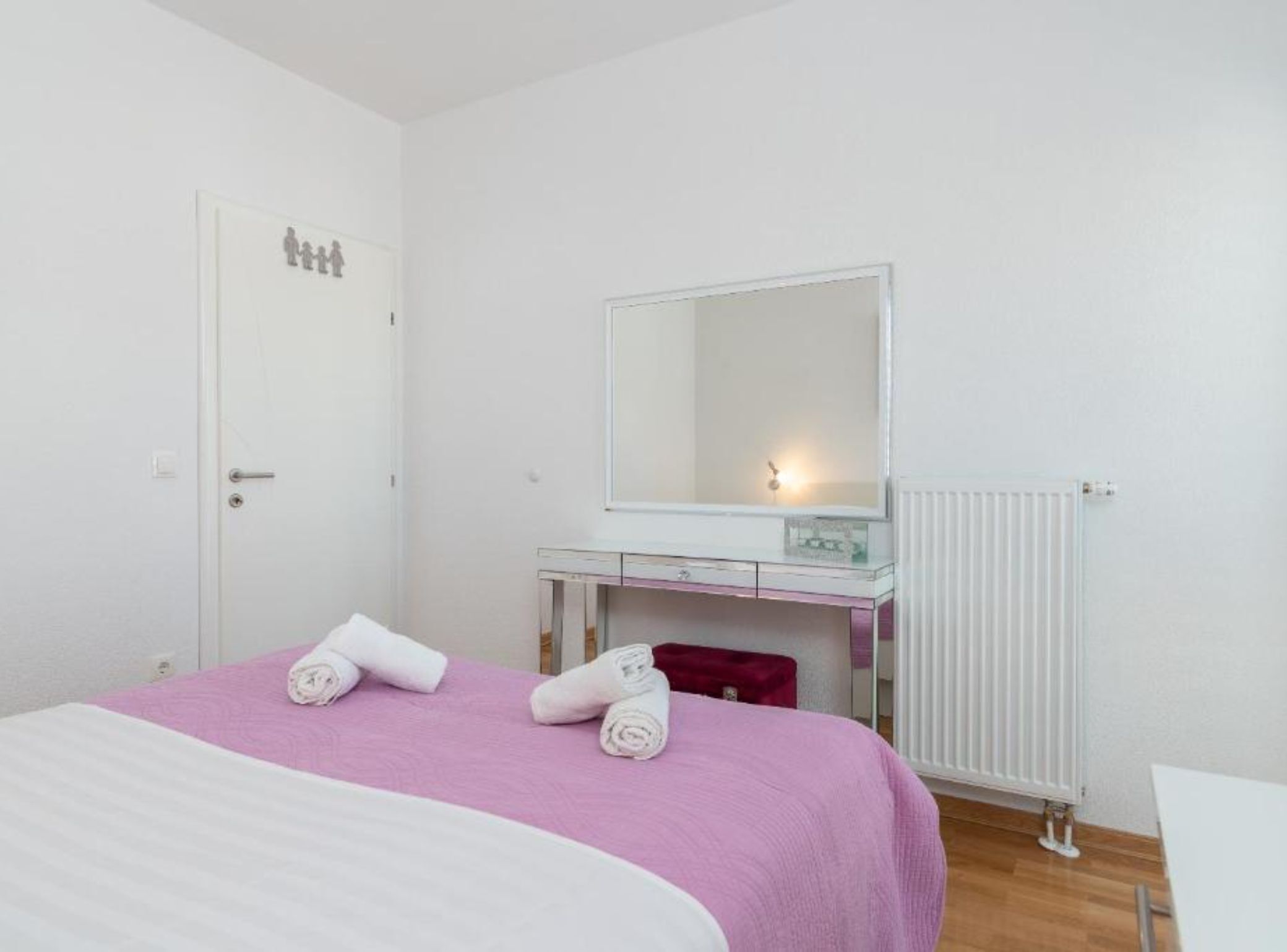 Quarto com cama, cômoda, espelho e radiador.
