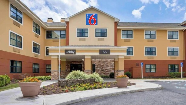 Um motel com um logotipo '6', entrada do saguão e uma placa com o número '55'.