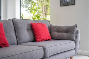 Um sofá modular cinza com almofadas vermelhas em um quarto com uma janela e um quadro na parede.