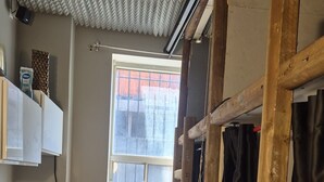 Um quarto com janela, vigas de madeira, uma prateleira branca e um armário branco.