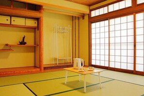 Um quarto japonês tradicional com tatames, uma mesa baixa com chaleira e xícaras, um cabideiro e portas deslizantes com padrão de grade.