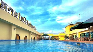 Piscina com céu azul límpido acima, rodeada por edifícios com varandas e áreas de estar ao ar livre.
