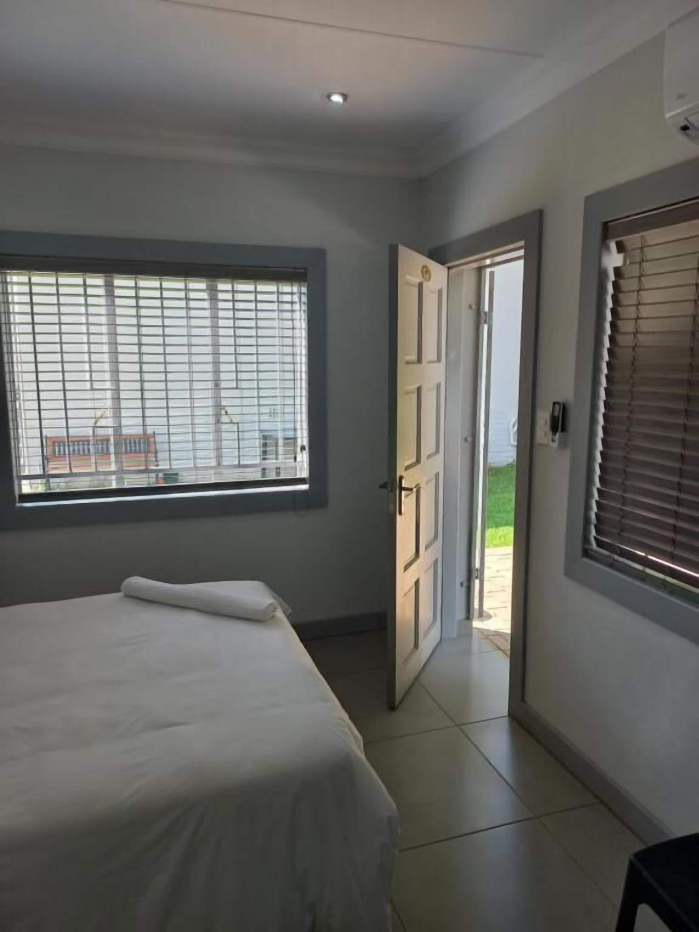 Quarto com cama, porta que dá para o exterior e janela com persianas.