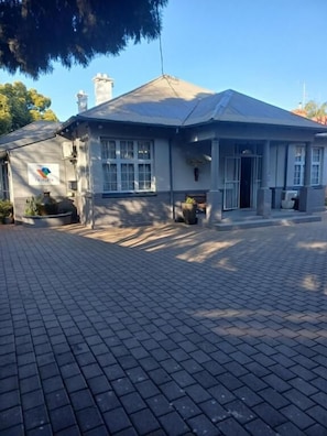 Um edifício com telhado de telhas, chaminé e área de entrada pavimentada.