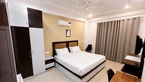Quarto de hotel com cama, escrivaninha, cadeira, guarda-roupa, televisão e ar condicionado.