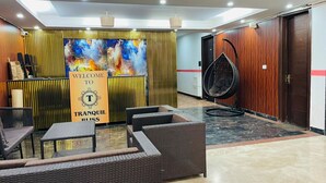 Uma área de recepção com uma placa de 'Bem-vindos ao Tranquil Triss', uma tela de TV grande, móveis de vime e uma cadeira suspensa.