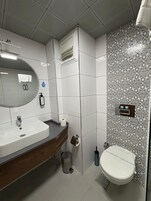Casa de banho com lavatório branco, espelho, sanita e azulejos estampados.