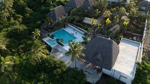 Um resort com piscina, cercado por vegetação exuberante e vários edifícios com telhados de palha.