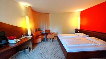 Quarto de hotel com cama, escrivaninha, cadeira e televisão.