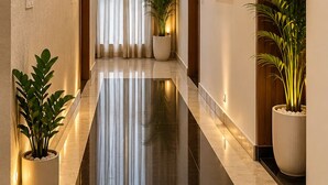 Um corredor moderno com piso espelhado, obras de arte emolduradas nas paredes e plantas em vasos.