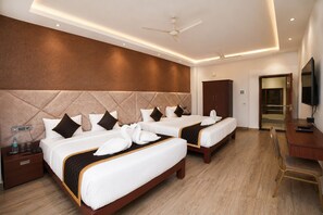 Quarto de hotel com duas camas, uma escrivaninha, uma televisão e um ventilador de teto.