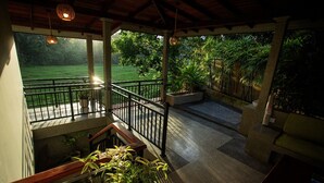 Área externa coberta com guarda-corpo de madeira, plantas em vasos e vista para uma paisagem verde.