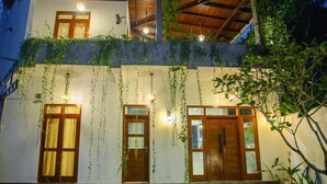 Um edifício de dois andares com portas de madeira, plantas penduradas e uma entrada bem iluminada.