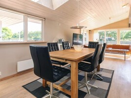 Uma área de jantar moderna com uma mesa de madeira, cadeiras estofadas em preto, um arranjo de vidro no centro e grandes janelas com vista para o verde.