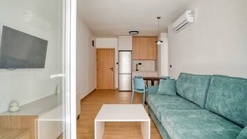 Uma sala de estar moderna com um sofá, uma mesa de centro e uma cozinha ao fundo.