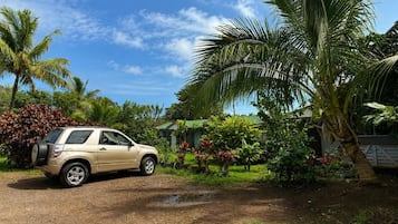 Um SUV bege estacionado em um caminho de terra, com uma casa e vegetação exuberante ao fundo.