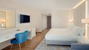 Quarto de hotel moderno com cama, escrivaninha, cadeira, televisão e luminária.