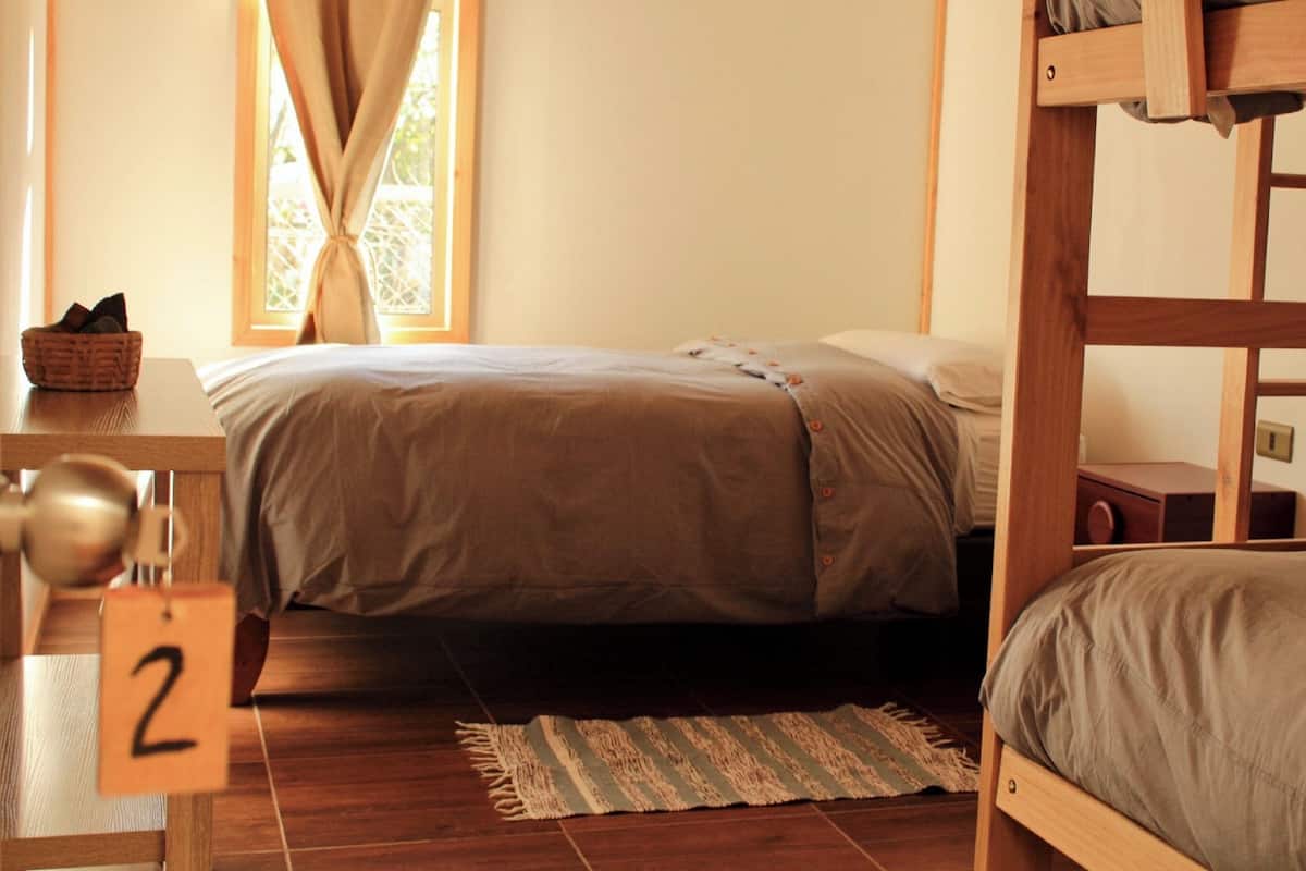 Quarto com duas beliches, uma escrivaninha de madeira, um cesto e um tapete.