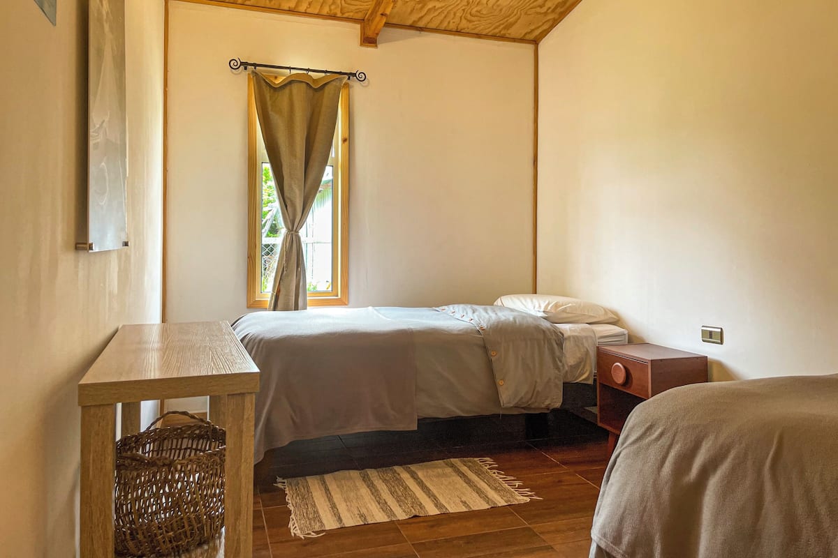 Quarto com cama, mesa de cabeceira e janela com cortinas.