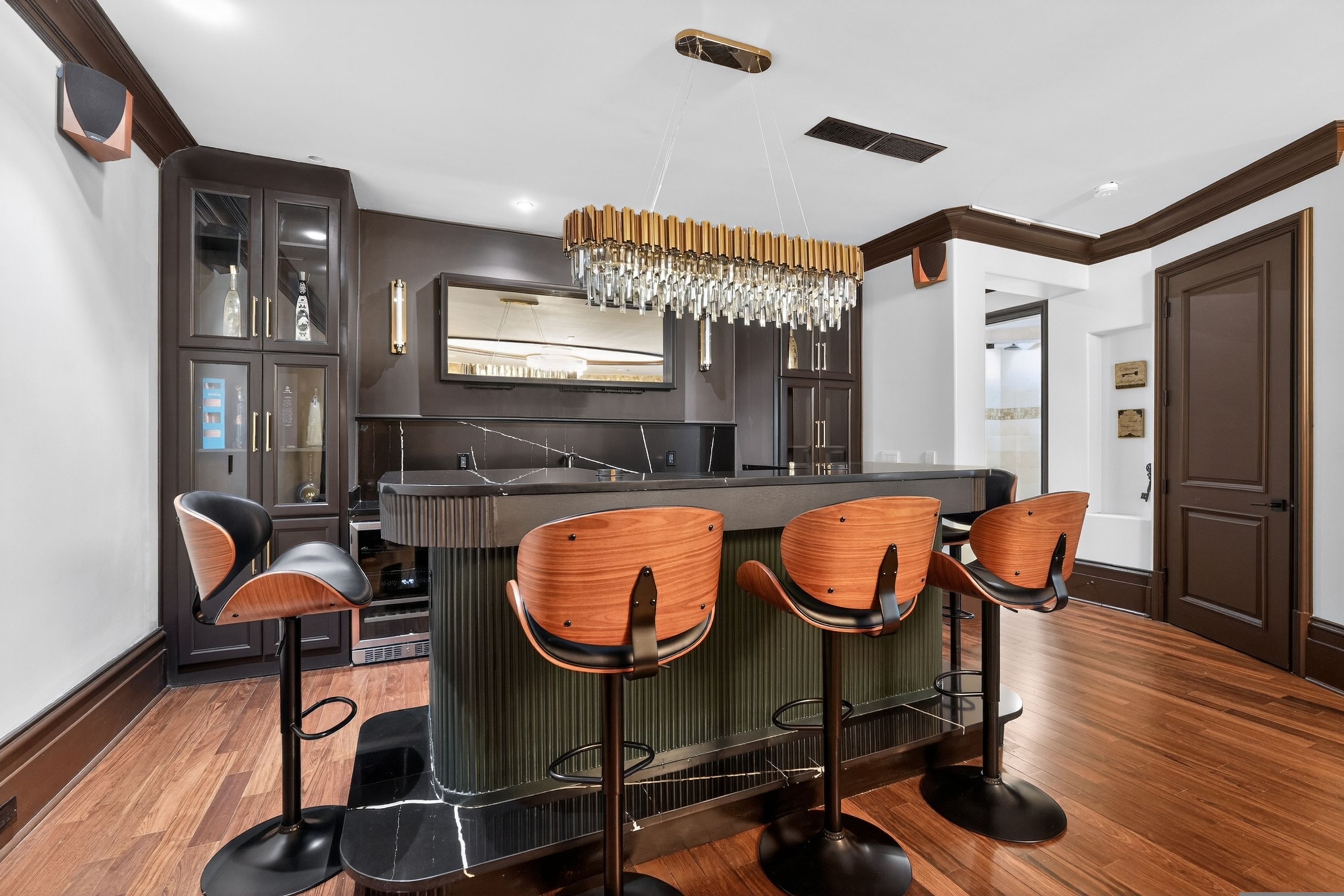 Uma cozinha moderna com armários escuros, uma ilha central com banquetas e um lustre.