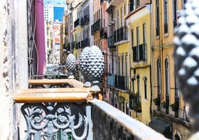 Uma rua estreita ladeada por edifícios, com um corrimão de metal com detalhes decorativos, e uma visão clara da rua.