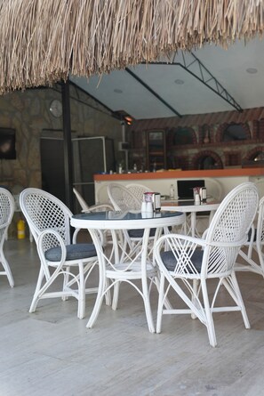 Restaurante com móveis de vime branco, uma mesa redonda e um telhado de palha.