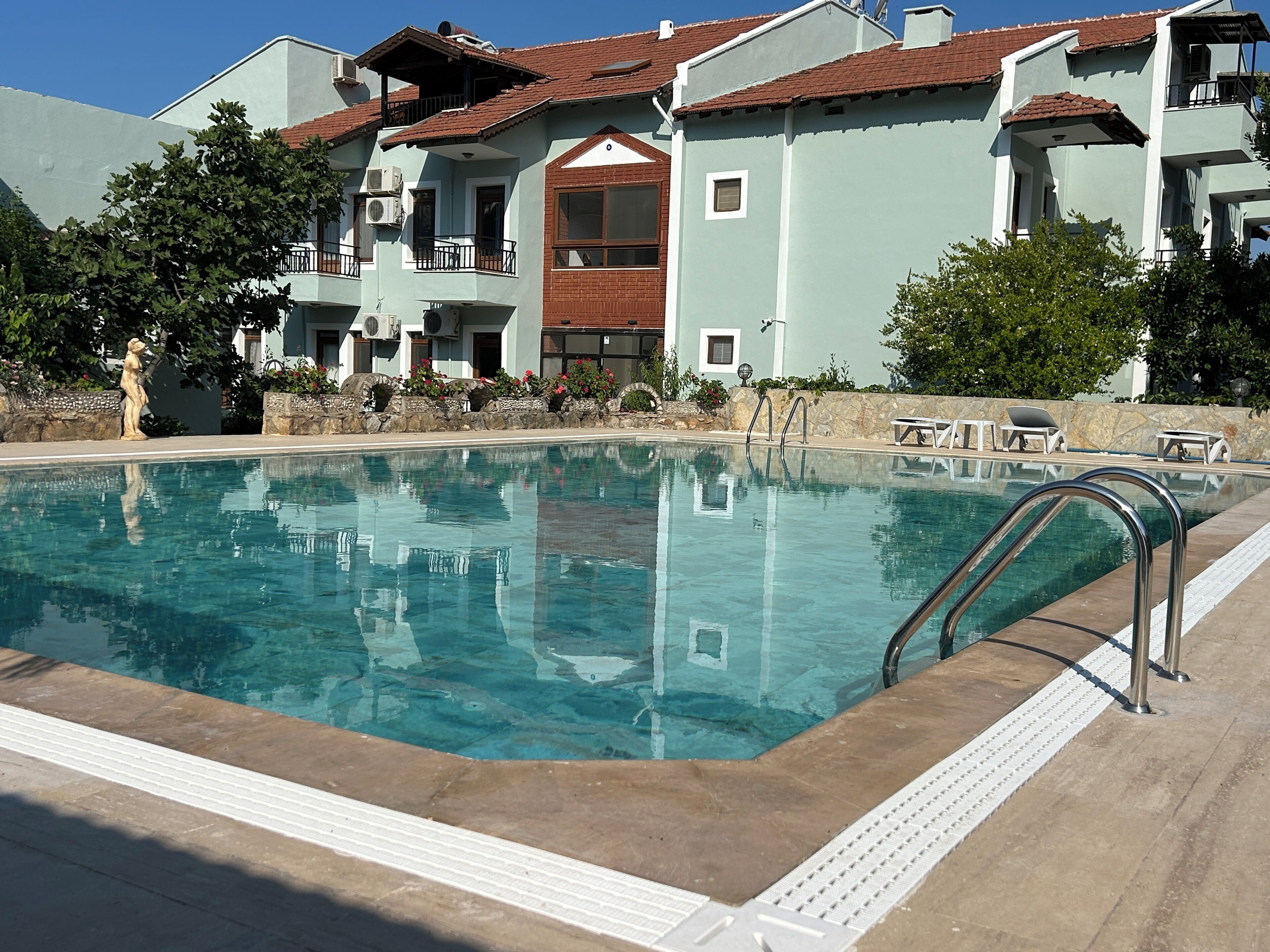 Piscina com água azul cristalina, ladeada por um deck de pedra e um baixo muro branco.