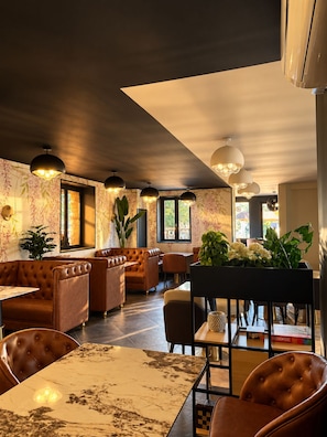 Interior de restaurante com assentos de couro, mesas de mármore e iluminação pendente.