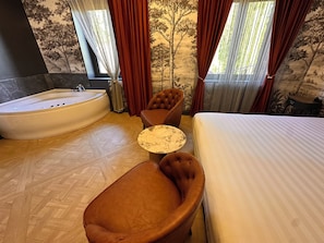 Quarto com uma banheira grande, cama, mesa redonda e poltrona de couro.