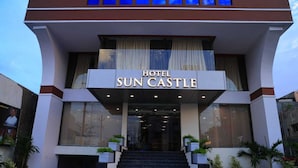 Entrada de hotel com uma placa indicando 'HOTEL SUN CASTLE', uma escadaria e plantas em vasos na base.
